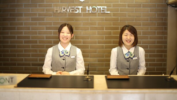 Duas recepcionistas no HARVEST HOTEL, com parede de tijolos ao fundo.