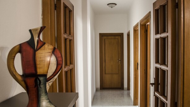 Um corredor com portas de madeira e um vaso decorativo sobre uma mesa.