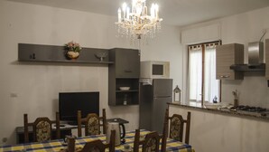 Uma área de refeições com toalha xadrez, cadeiras de madeira, um candelabro, uma televisão, um frigorífico e um micro-ondas.