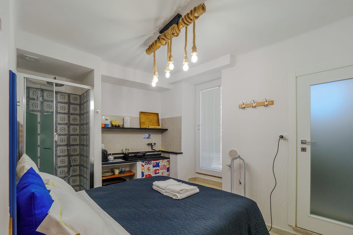 Quarto com cama, banheiro com chuveiro e uma cozinha compacta.