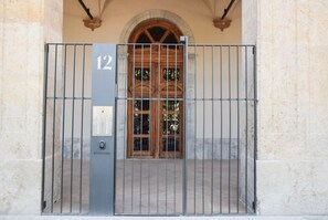 Uma entrada fechada por portão, com a placa de número 12, um portão de metal e uma porta de madeira com painéis de vidro.