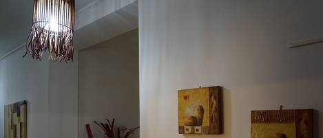 Um corredor com obras de arte nas paredes, uma luminária pendente e um vaso de planta.