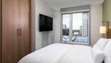 Quarto de hotel com uma cama grande, uma TV fixada na parede e uma janela com vista para a cidade.