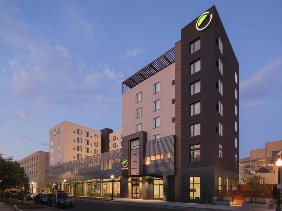 Um hotel moderno com um logotipo marcante na fachada, vários andares e uma entrada bem iluminada.
