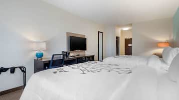Quarto de hotel com duas camas, uma escrivaninha com computador, televisão e uma luminária.