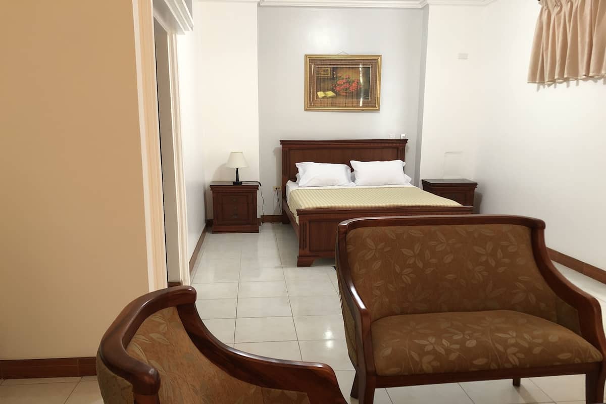 Quarto com cama, duas mesas de cabeceira, luminária, poltrona e um quadro na parede.