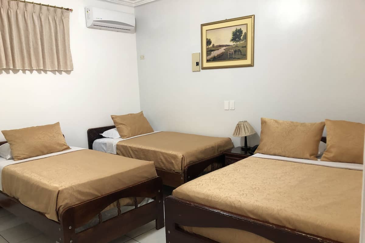 Quarto de hotel com três camas, um quadro na parede, ar-condicionado e uma cortina.
