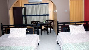 Quarto de hotel com duas camas, uma mesa de jantar, cadeiras, uma mesinha com um vaso de flores e um aparelho de ar condicionado.
