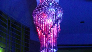 Um lustre decorativo com vários níveis e elementos pendentes, suspenso no teto de um ambiente com pouca luz.