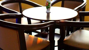 Mesa redonda com um vaso branco contendo flores vermelhas, rodeada por cadeiras de madeira.