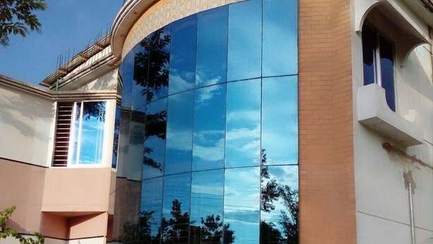 Um edifício moderno com fachada de vidro curva refletindo o céu e as árvores.