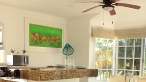 Cozinha moderna com bancada de granito, dois banquetes verde-água, ventilador de teto e janela com vista para o verde.