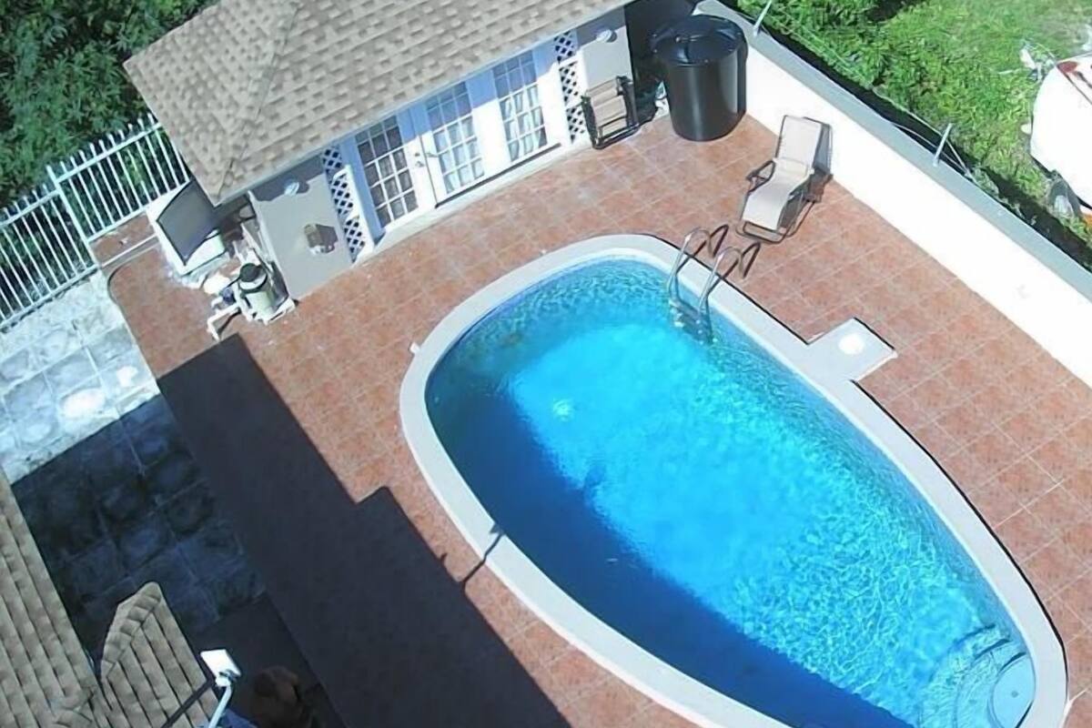 Piscina com deck revestido, área de estar coberta e quintal cercado.