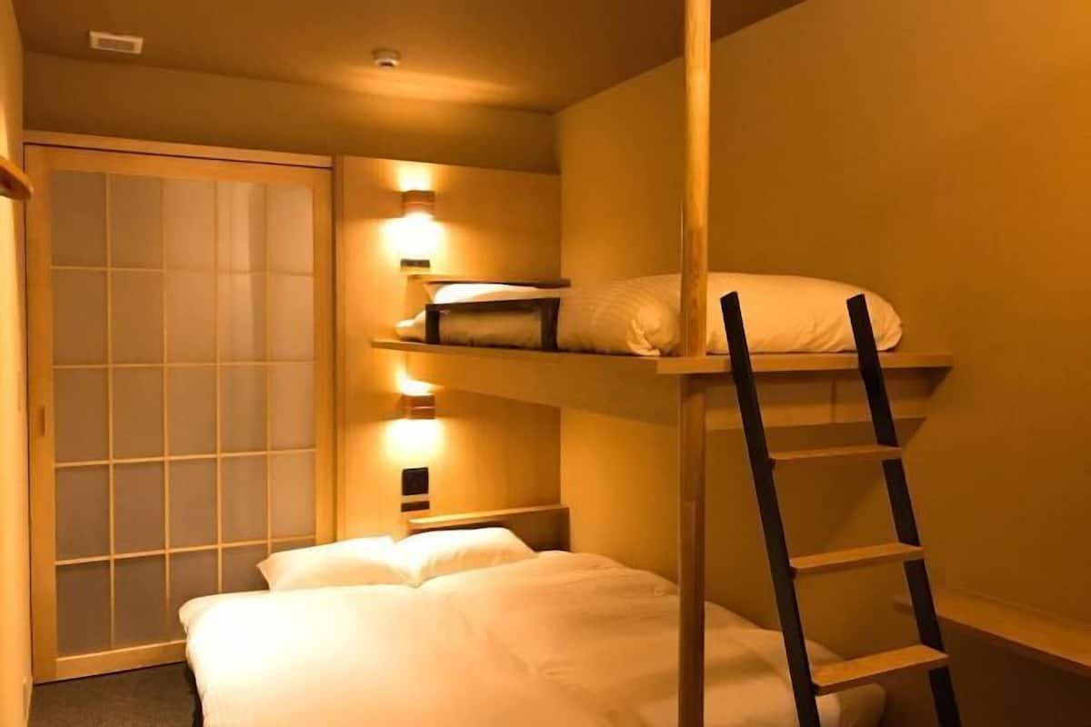 Quarto com beliche, uma escada, porta deslizante e luminárias fixadas na parede.