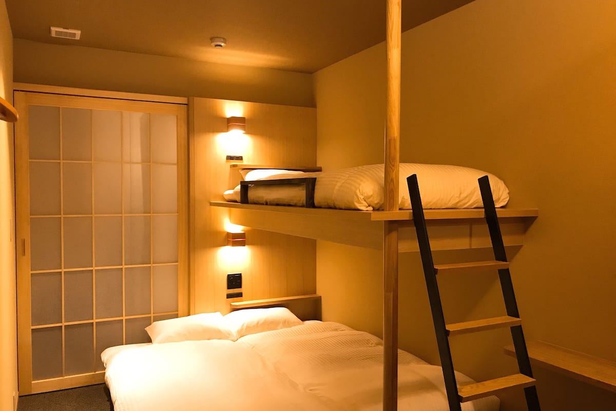 Uma cama de beliche com escada, mesa de cabeceira e luminária fixada na parede.