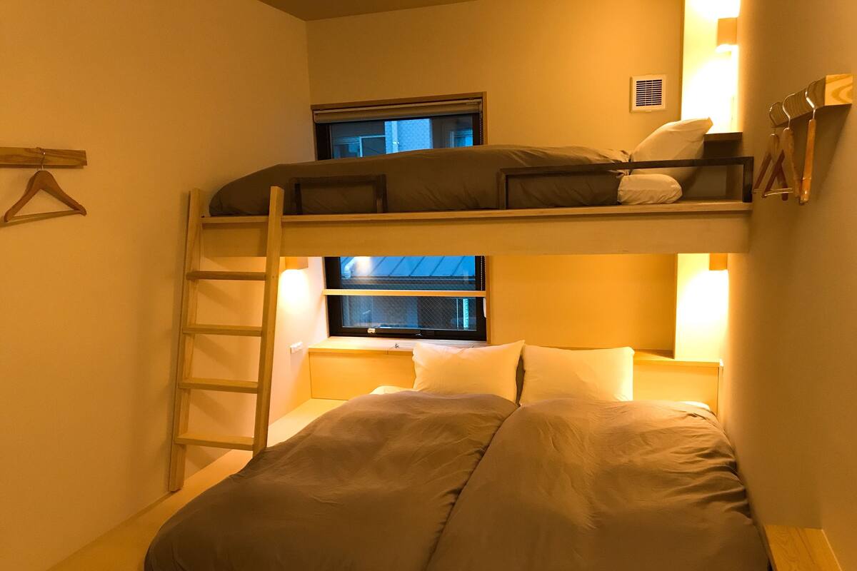 Uma cama beliche com escada, janela e mesa de cabeceira com abajur.