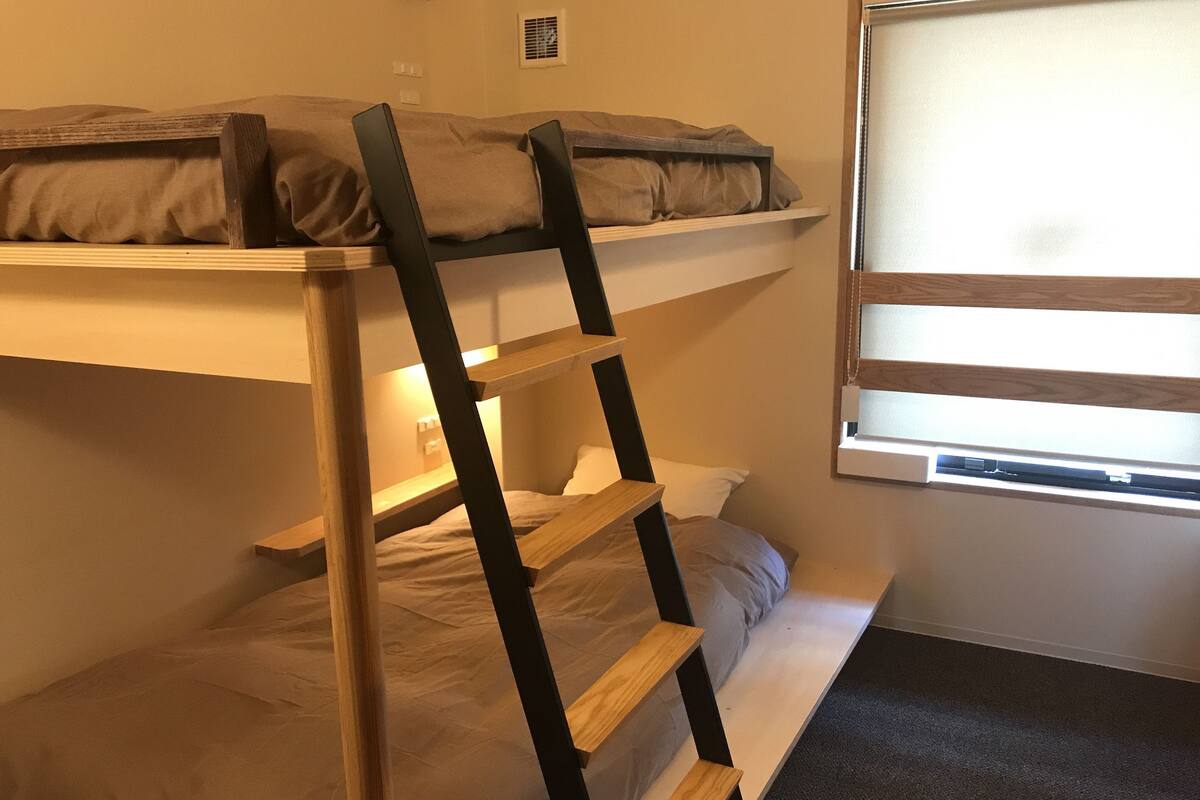 Quarto com beliche, uma janela e uma pequena abertura na parede.
