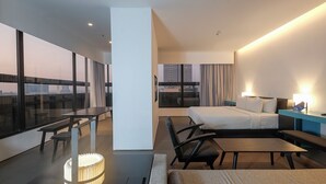 Quarto de hotel moderno com uma janela grande, uma cama, uma mesa e uma cadeira.
