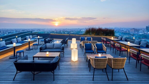 Terraço no telhado com áreas de estar, mesas e vista do horizonte urbano ao pôr do sol.