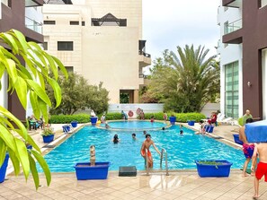 Uma área de piscina com várias piscinas, rodeada por edifícios e vegetação.