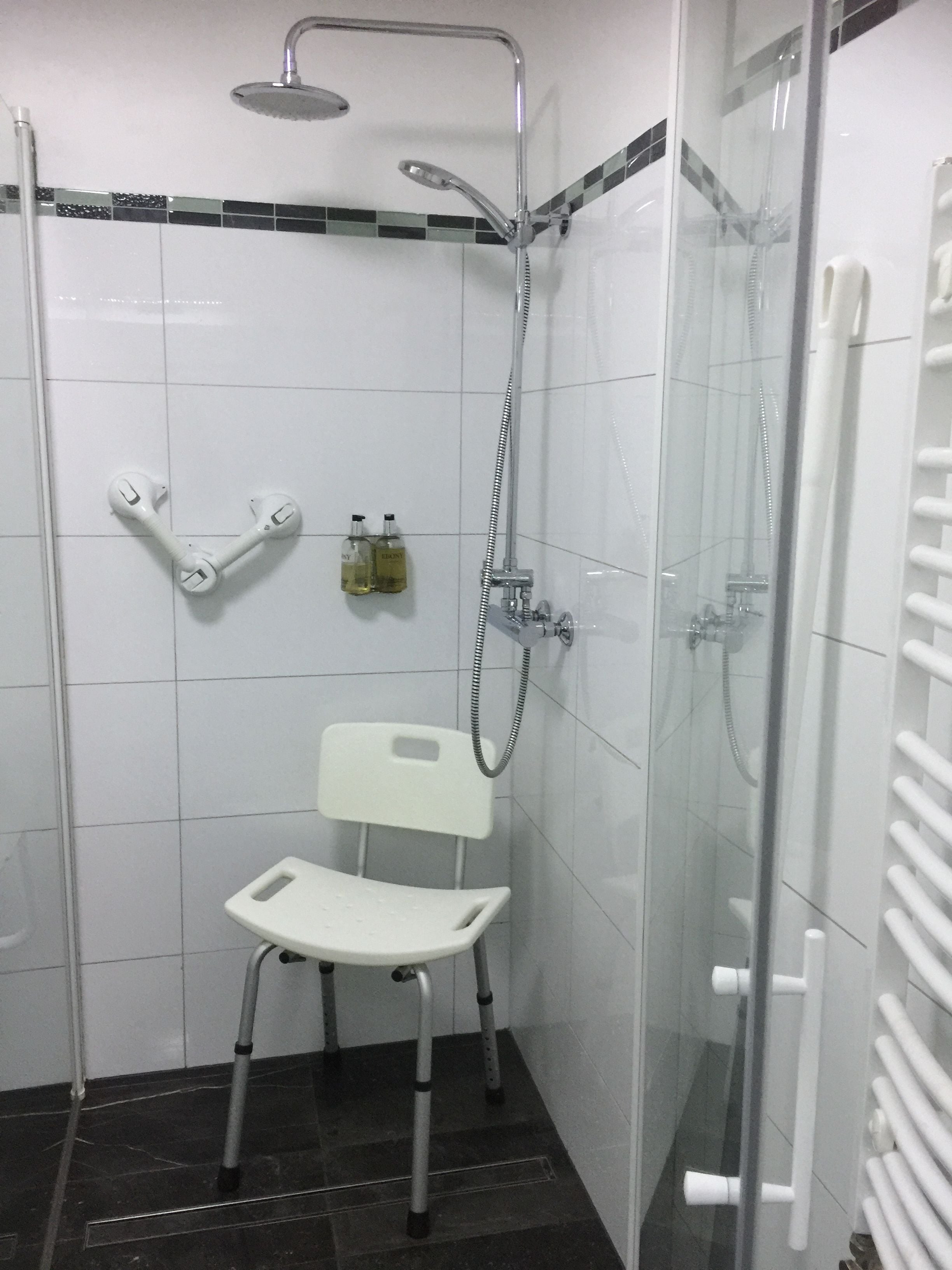 Uma área de chuveiro com porta de vidro, uma cadeira branca e um secador de mãos.