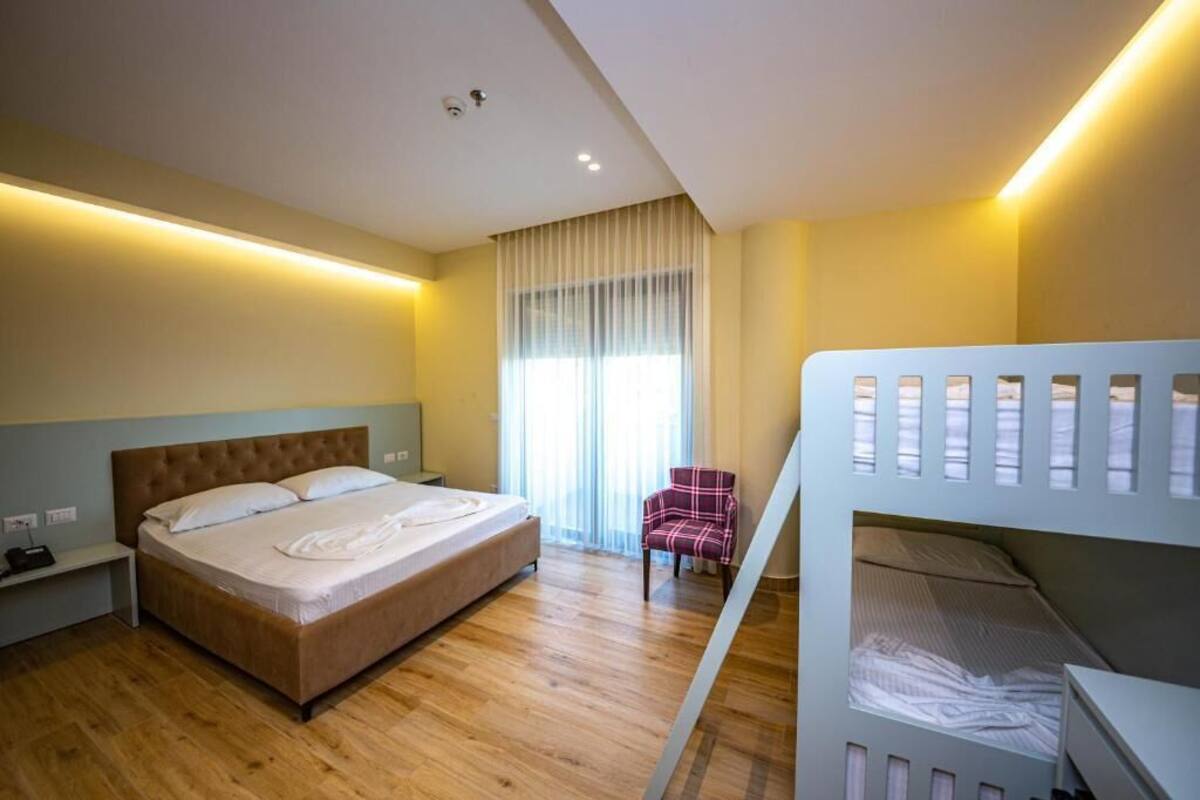 Quarto com uma cama grande, uma cama menor, uma cadeira e uma beliche.