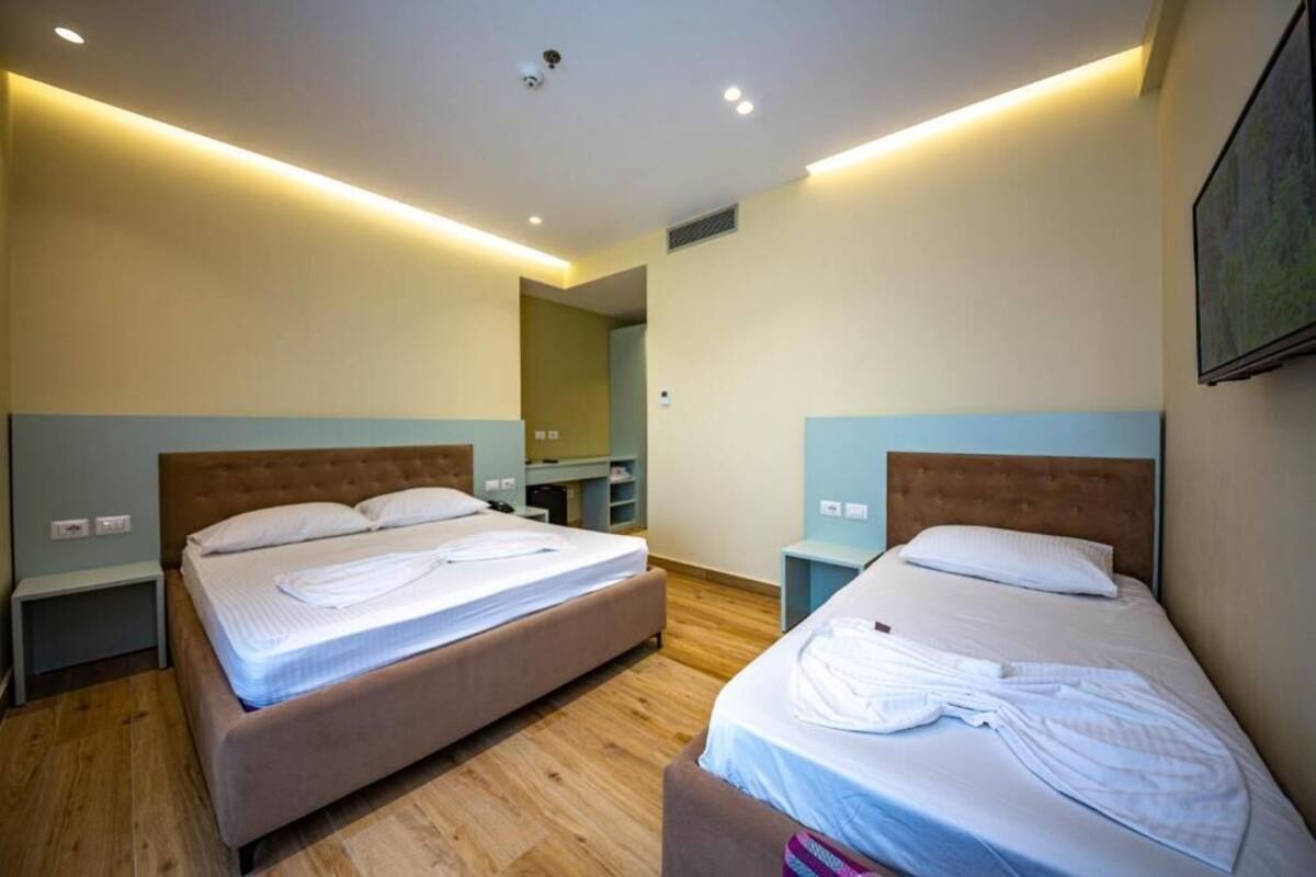 Quarto de hotel com duas camas, assoalho de madeira e um espelho grande na parede.