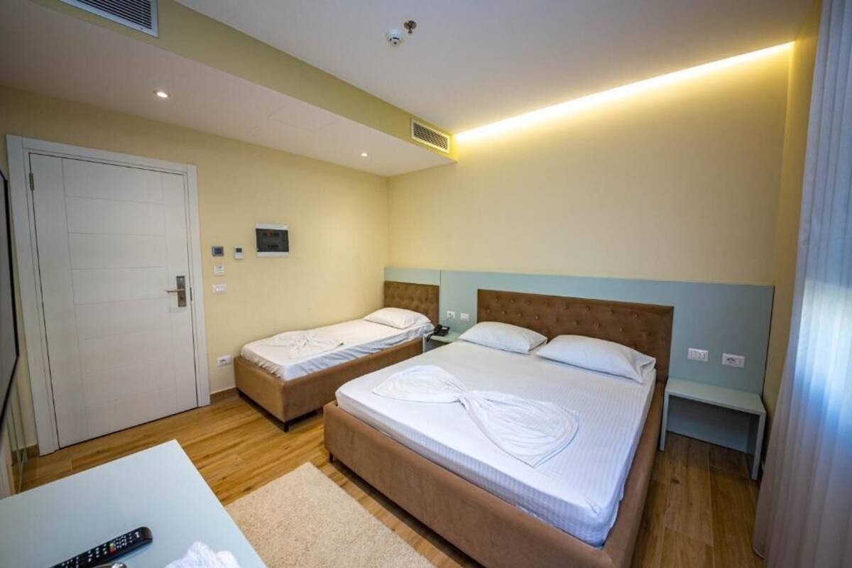 Quarto de hotel com duas camas de solteiro, uma pequena mesa, uma cadeira e uma porta.