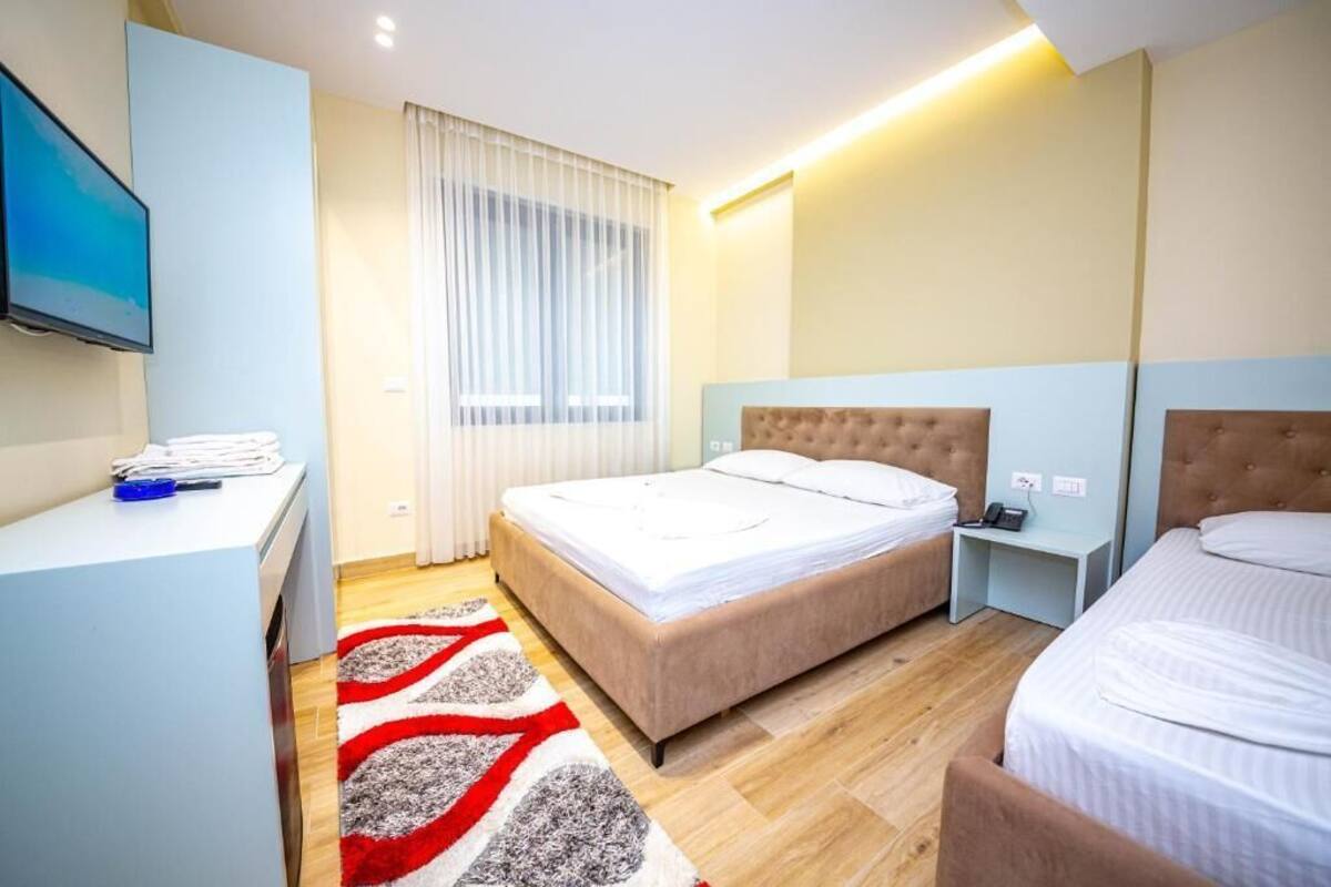 Quarto de hotel com uma cama, mesa de cabeceira e televisão presa na parede.