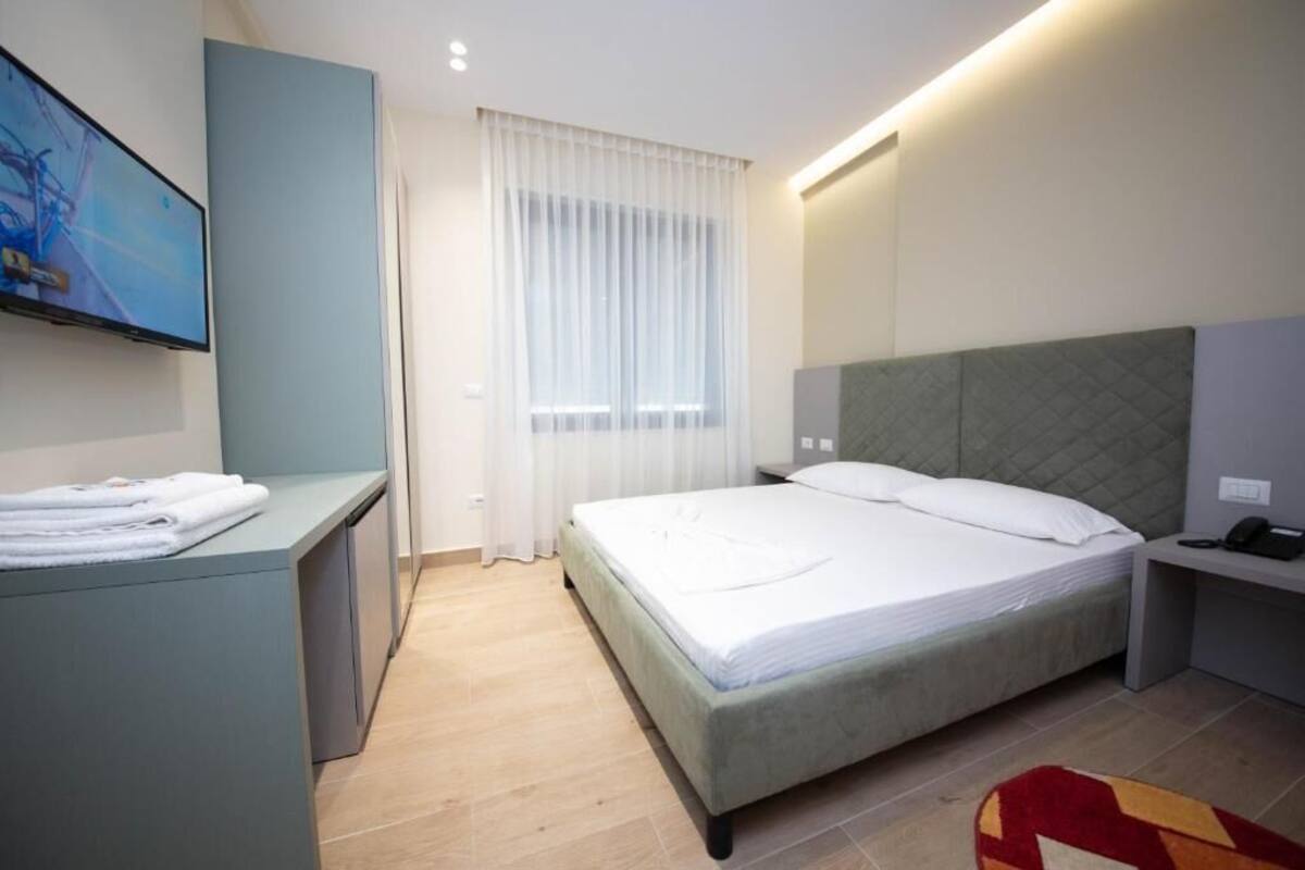 Quarto de hotel moderno com cama, escrivaninha, televisão e janela com cortinas.