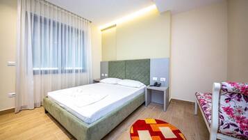 Quarto de hotel com cama, mesa de cabeceira, cadeira e tapete estampado.