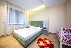 Quarto de hotel com cama, mesa de cabeceira, cadeira e tapete estampado.