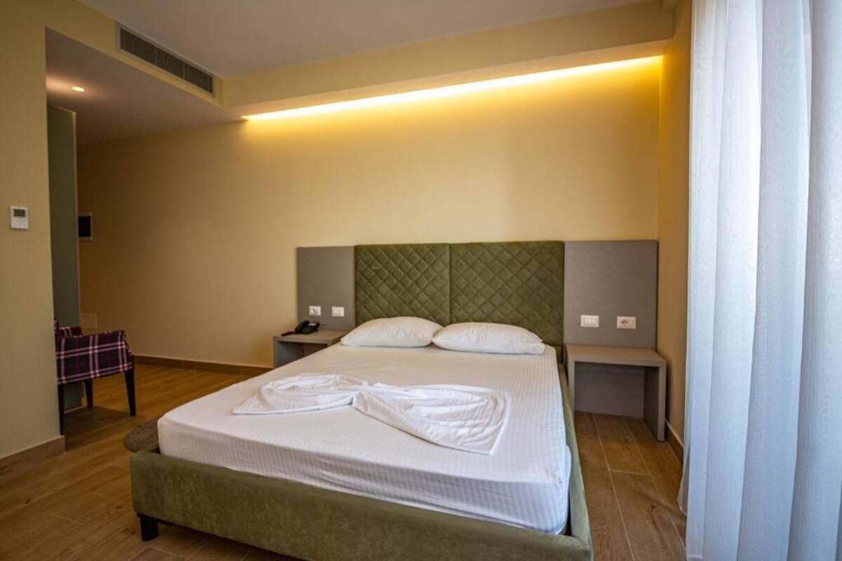 Quarto de hotel com cama, mesinhas de cabeceira, um banco e um criado-mudo.
