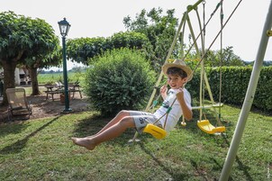 Criança num balanço, num jardim com um poste de luz e um banco ao fundo.