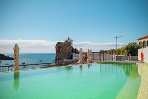 Piscina com vista para o mar e formação rochosa com farol.