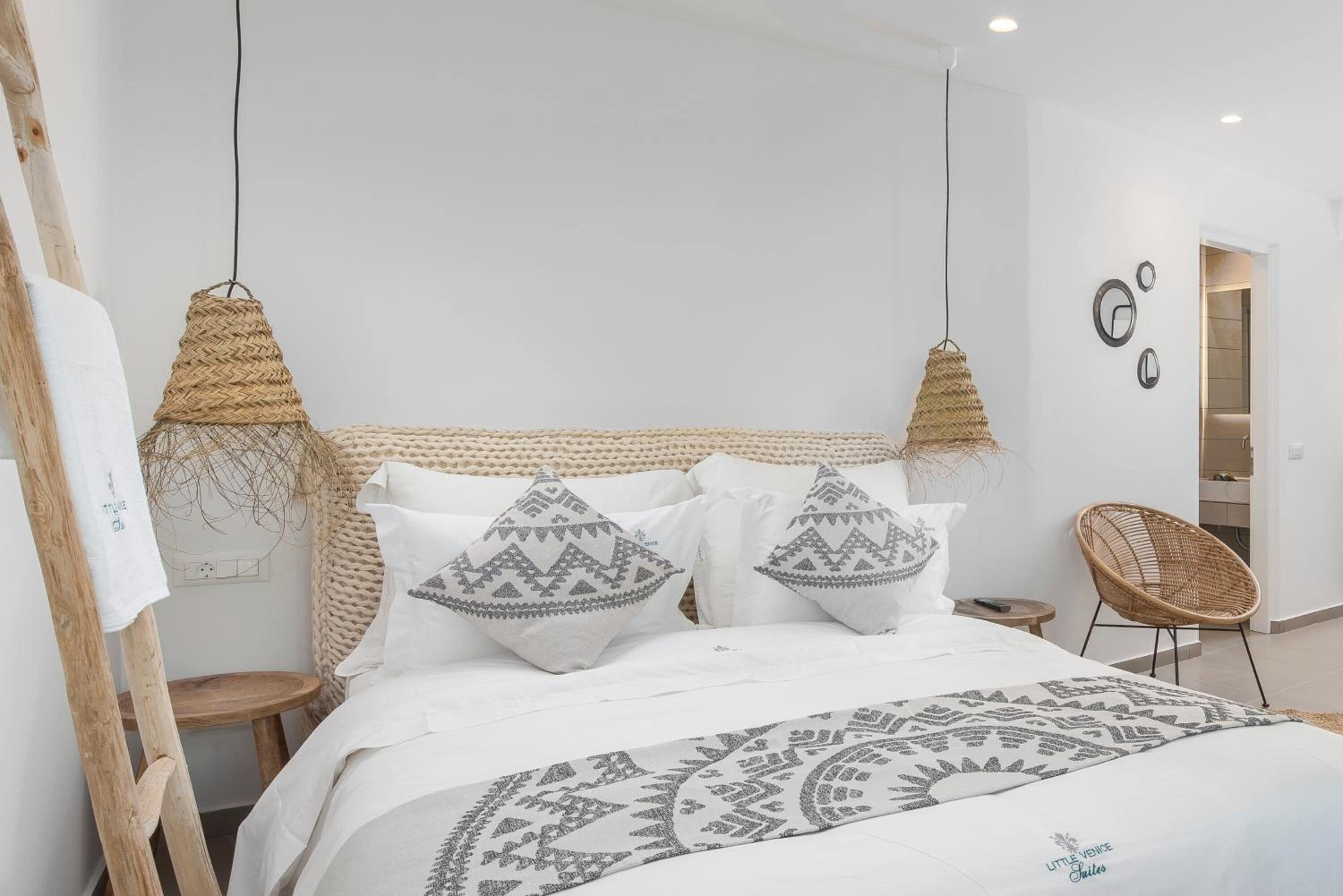 Quarto moderno com cama branca, manta estampada, luminárias de fibra e cadeira de vime.