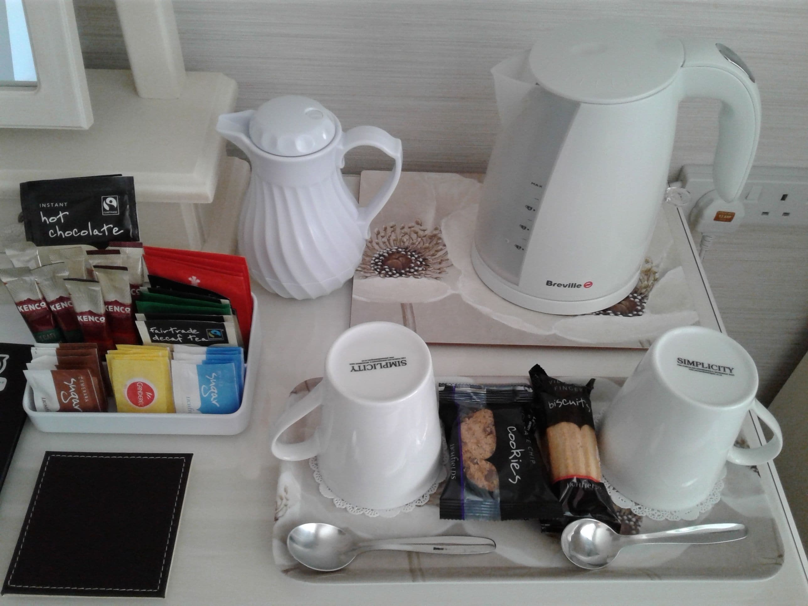 Uma mesa de pequeno-almoço com máquina de café, bule, chávenas e diversas comidas.