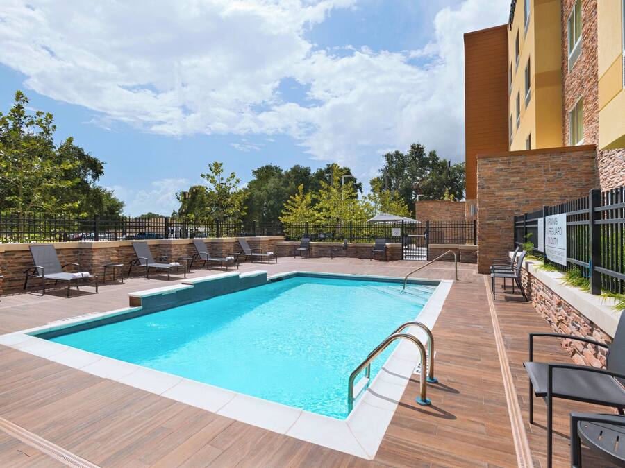 Piscina retangular com deck ladrilhado, rodeada por espreguiçadeiras e uma parede de pedra.