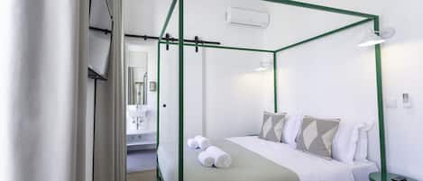 Quarto de hotel moderno com cama de dossel, parede verde de destaque, mesa de cabeceira e um espelho.