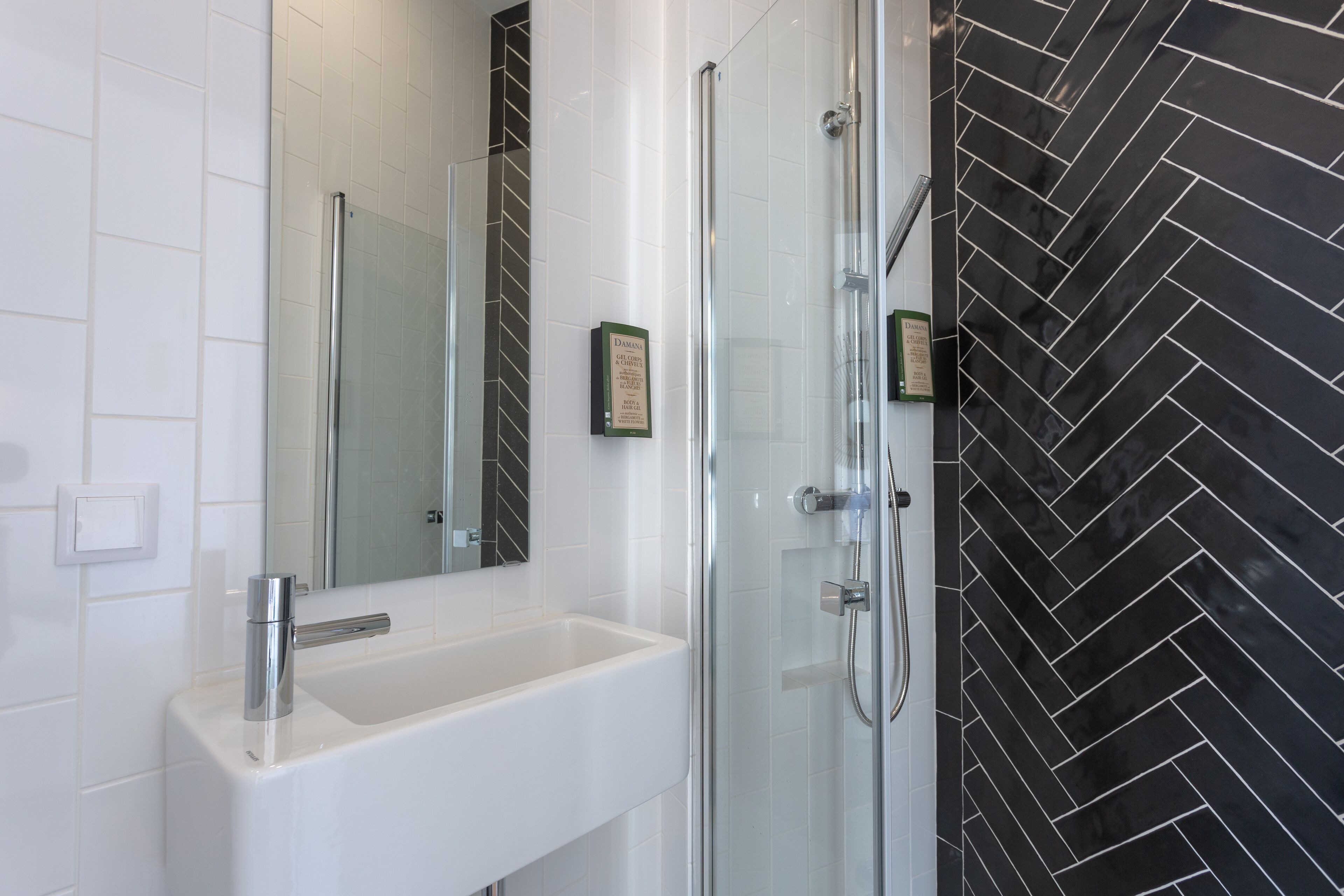 Casa de banho com lavatório branco, cabine de chuveiro em vidro e azulejos em padrão losango preto e branco.