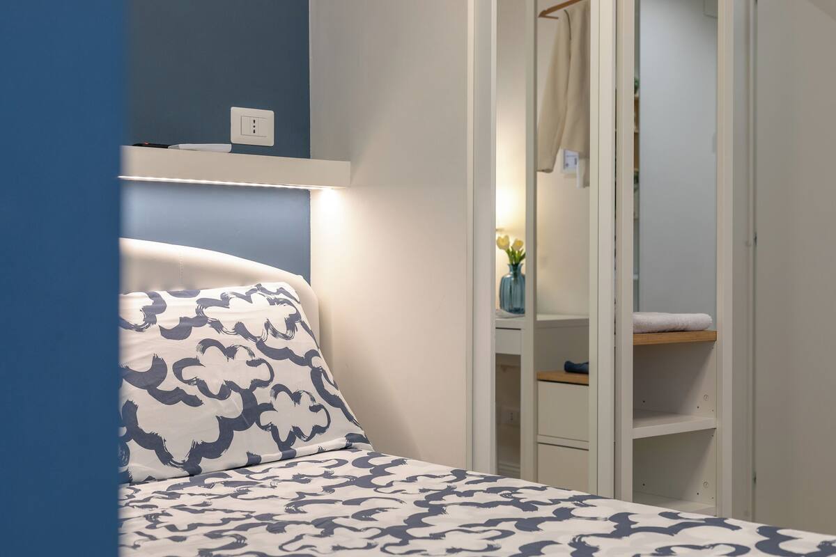 Quarto com cama, mesa de cabeceira, espelho e guarda-roupa.