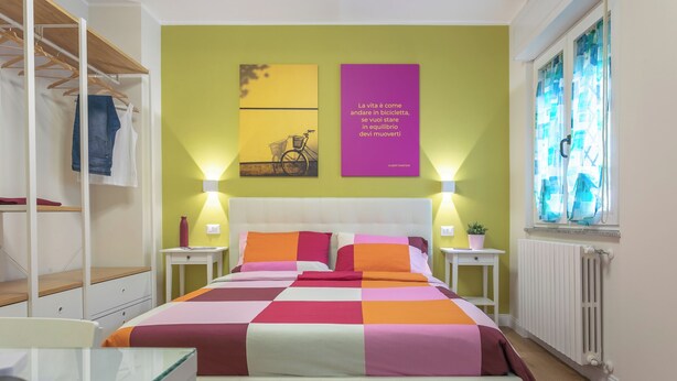 Quarto com cama, duas mesas de cabeceira, guarda-roupa e janela com cortinas.