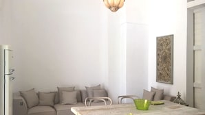 Uma sala de jantar com uma mesa de madeira, cadeiras, uma tigela verde e um sofá com almofadas.