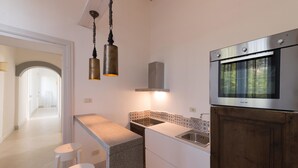 Cozinha moderna com forno embutido, pia e bancada. Há duas banquetas e um pendente.