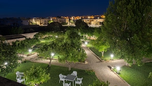 Vista noturna de um pátio com mesas ao ar livre e um edifício ao fundo.