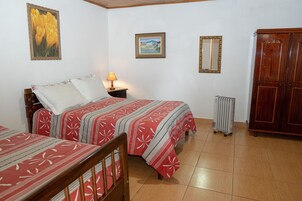 Quarto com duas camas, mesa de cabeceira, abajur, radiador e guarda-roupa.