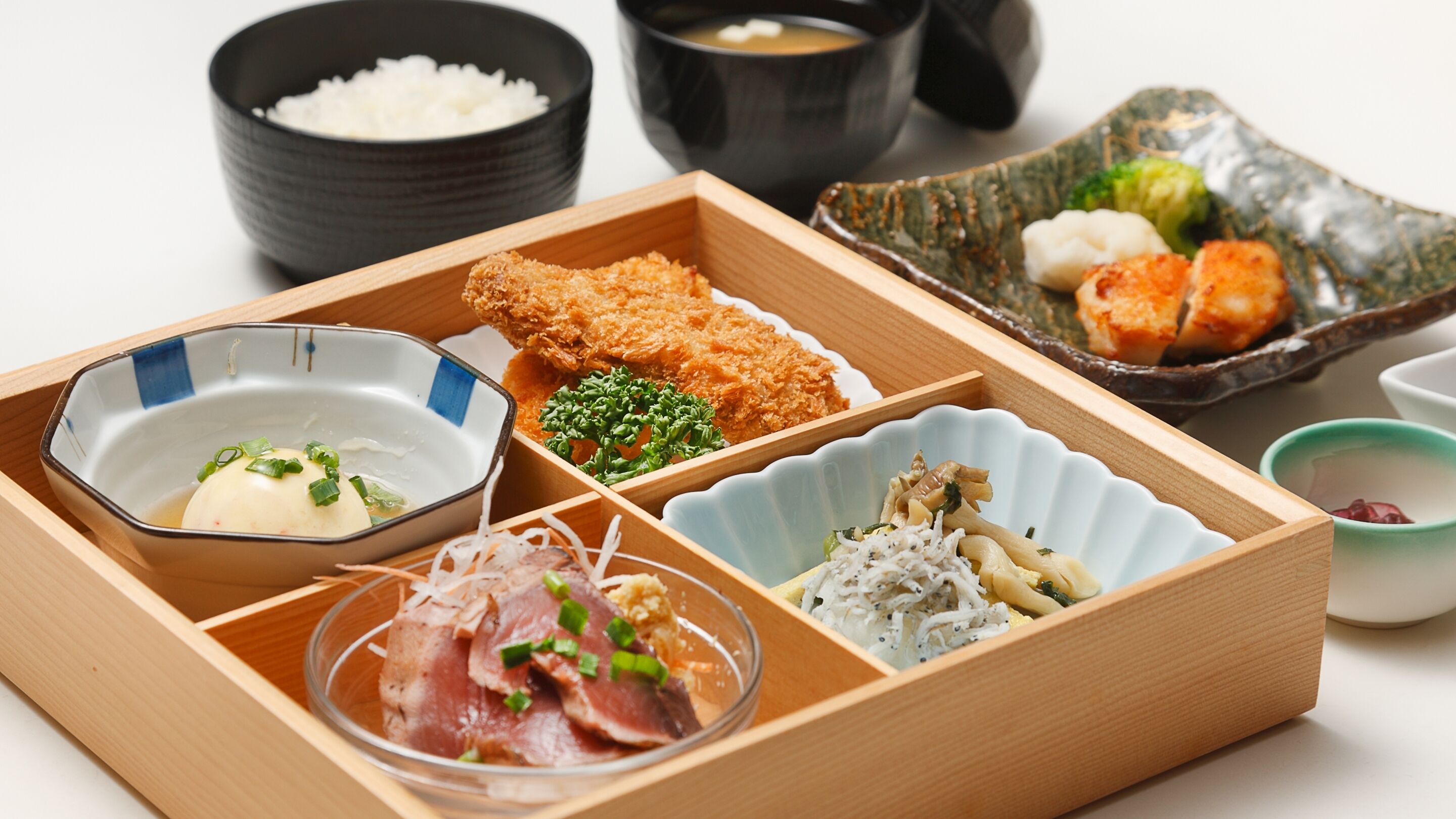Uma refeição tradicional japonesa com diversos pratos dispostos em compartimentos distintos de uma bandeja de madeira.