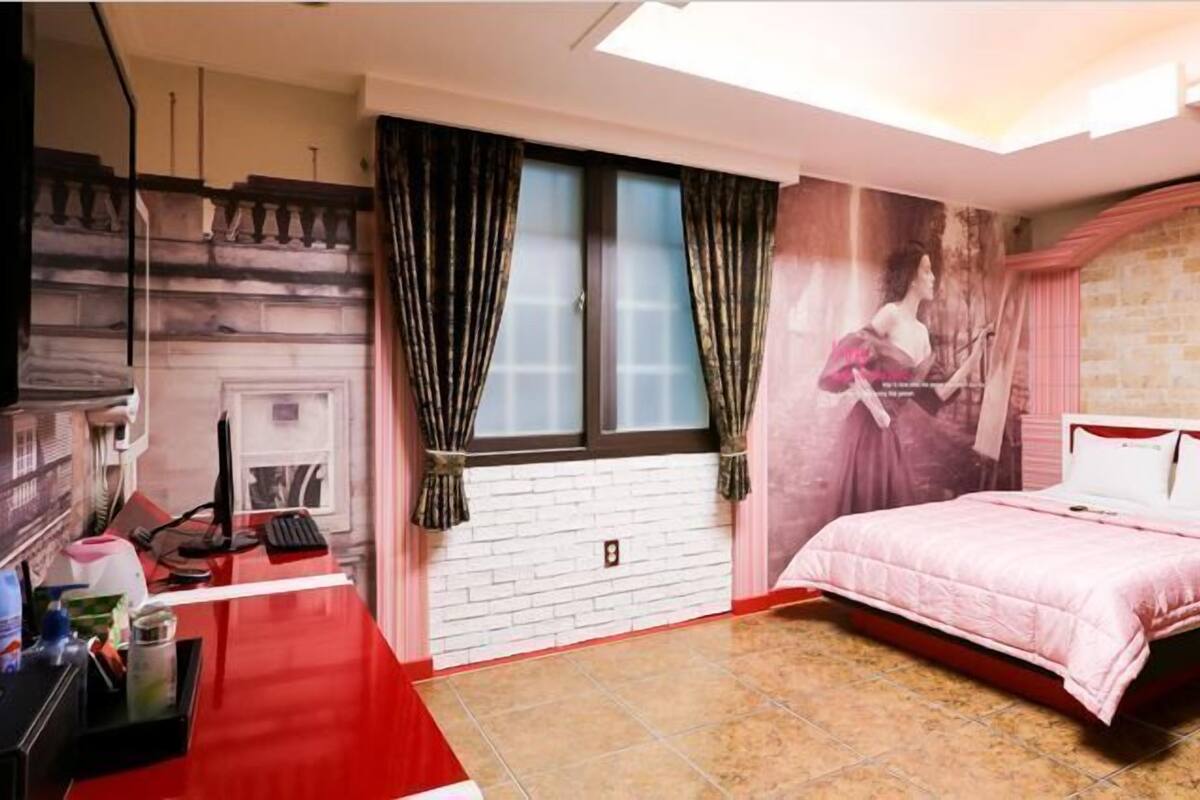 Quarto com cama, escrivaninha, cadeira, mesa de cabeceira e parede com mural.