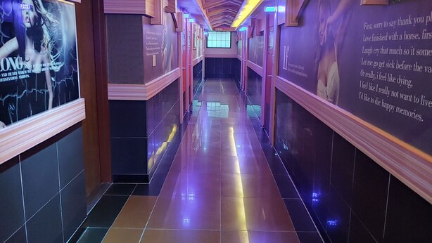 Um corredor com pisos de azulejos refletivos, painéis de madeira e placas iluminadas.