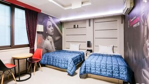 Quarto de hotel com duas camas, uma mesinha, uma cadeira e um pôster grande na parede.